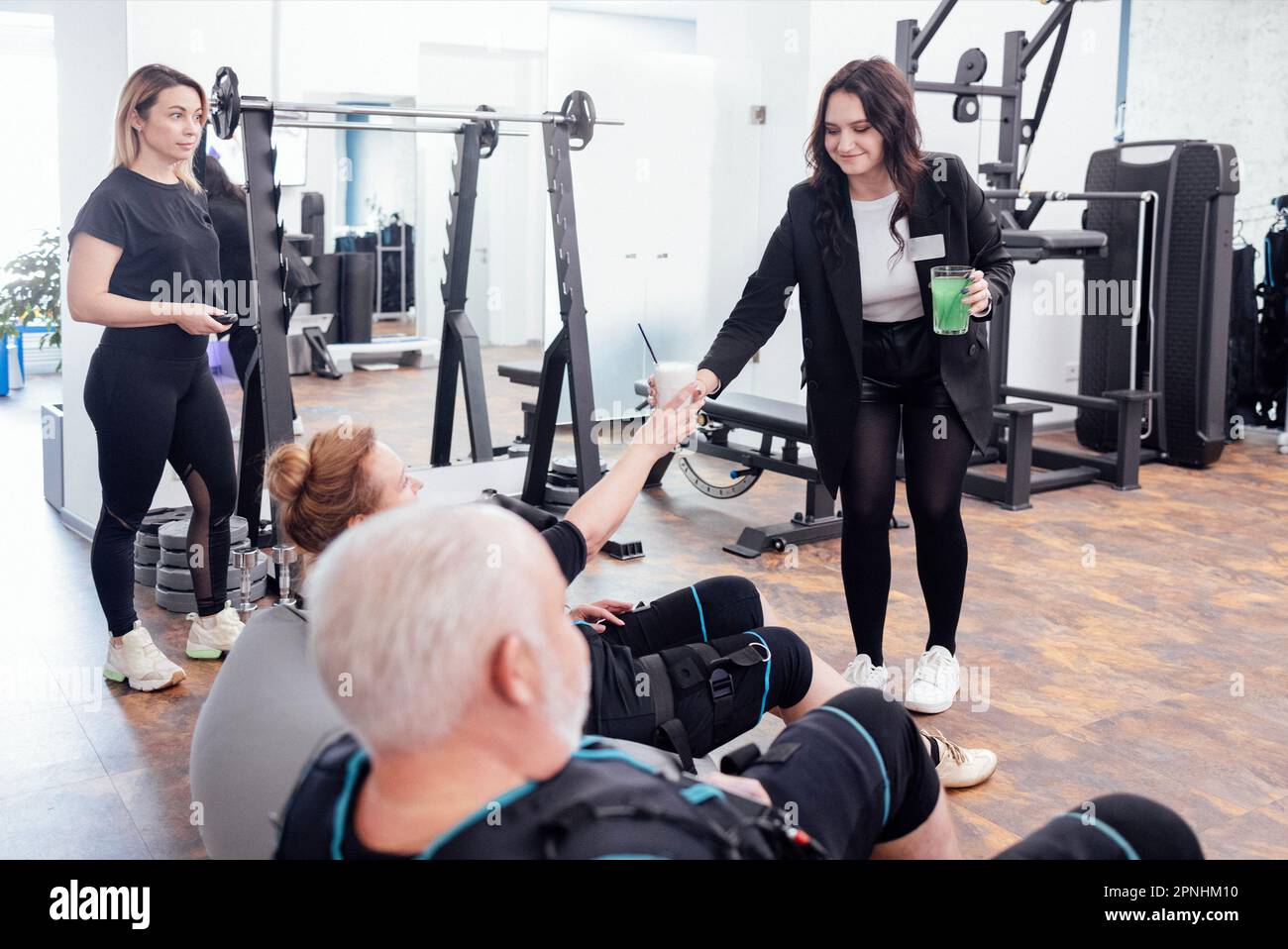 Smiling female gym worker gives freshly made cocktail to elderly client ...