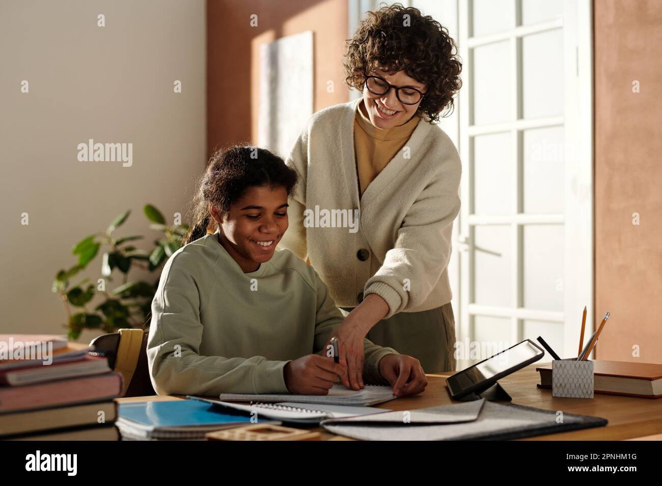 Smiling young mother pointing at textbook and explaining the topic to ...