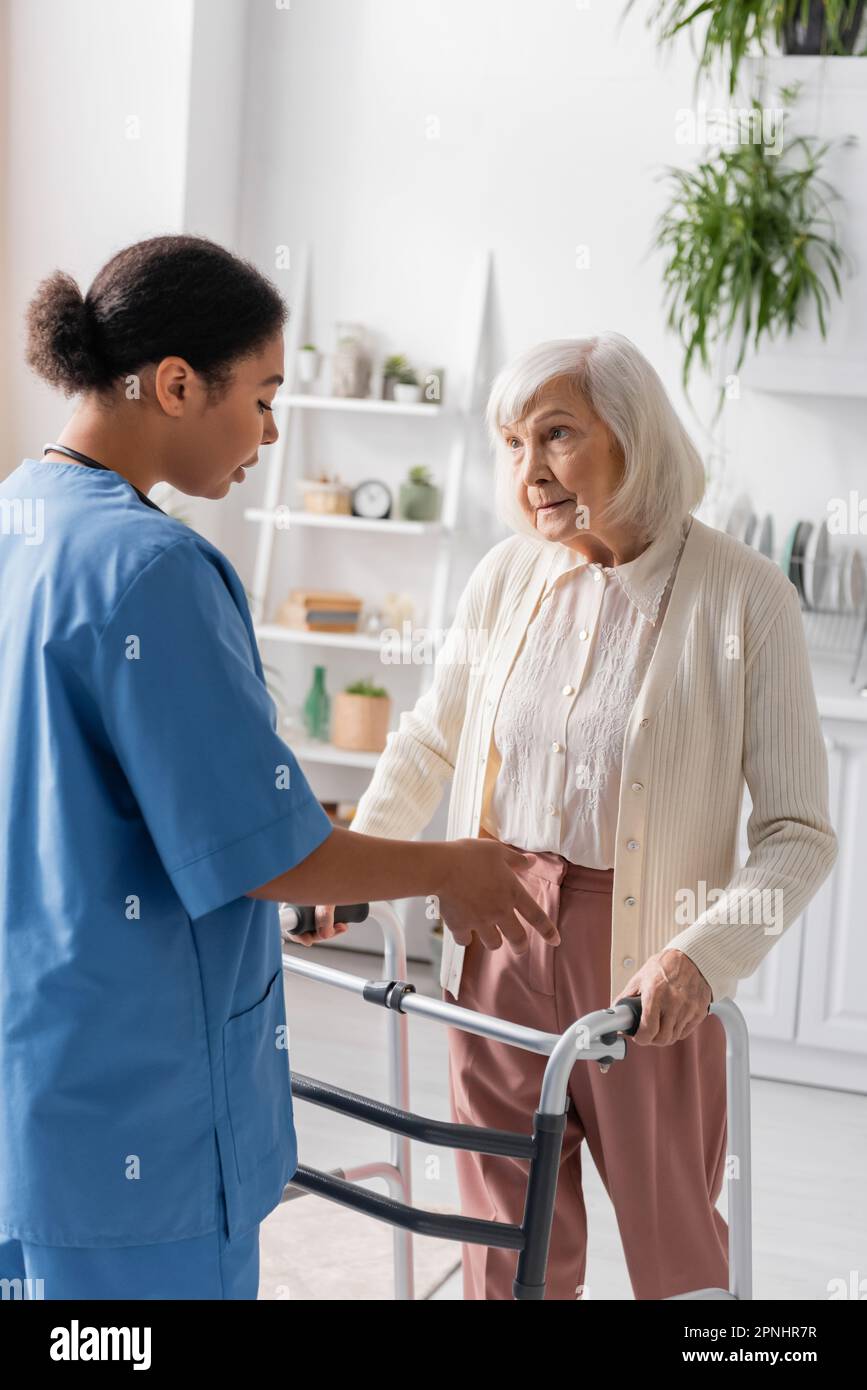 senior woman with grey hair walking with help of walker and looking at ...