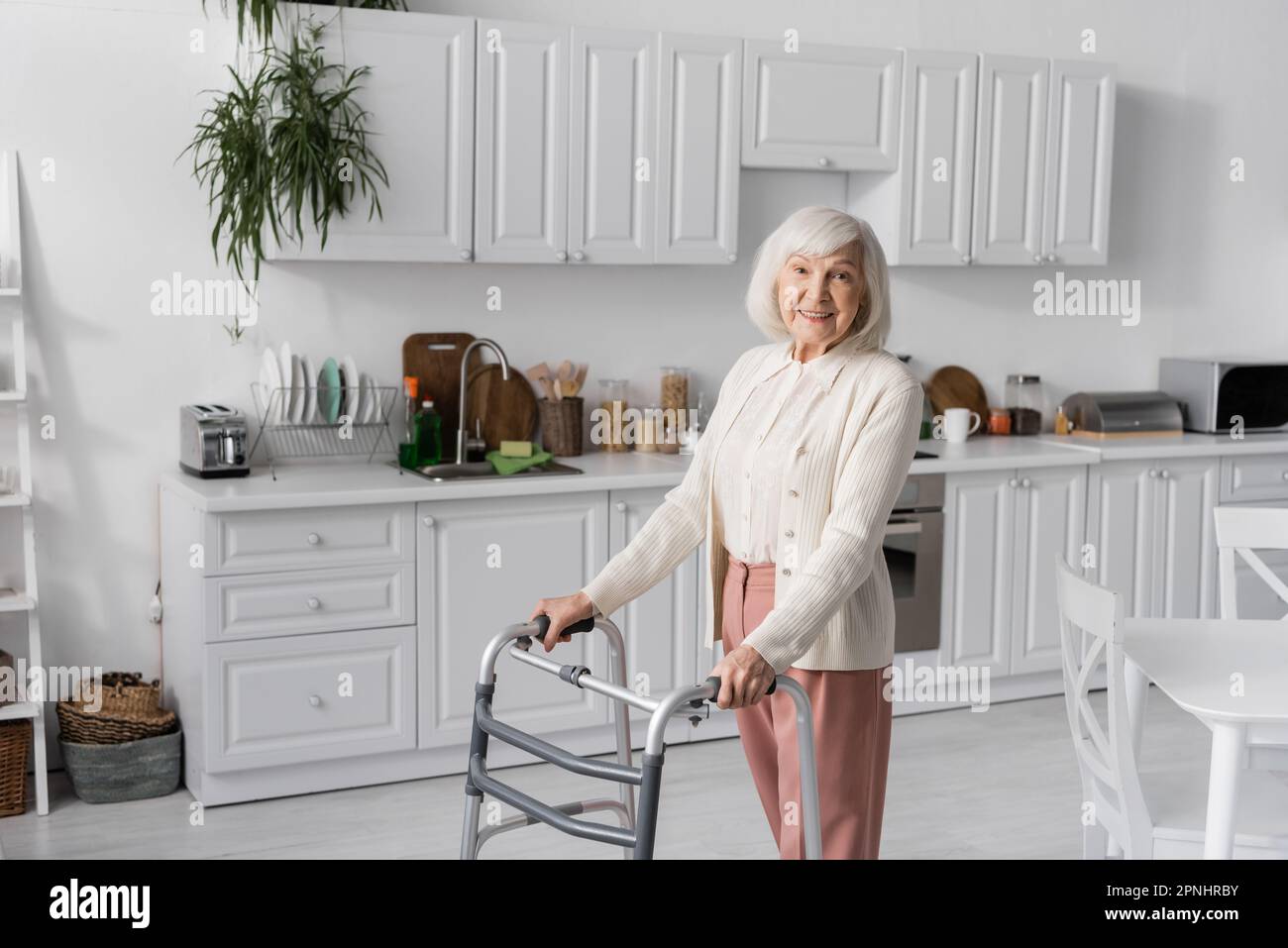 positive senior woman with grey hair walking with help of walker in ...