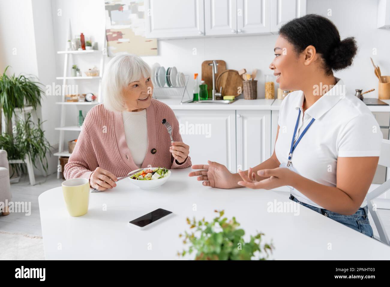 happy senior woman with grey hair eating salad and talking with ...