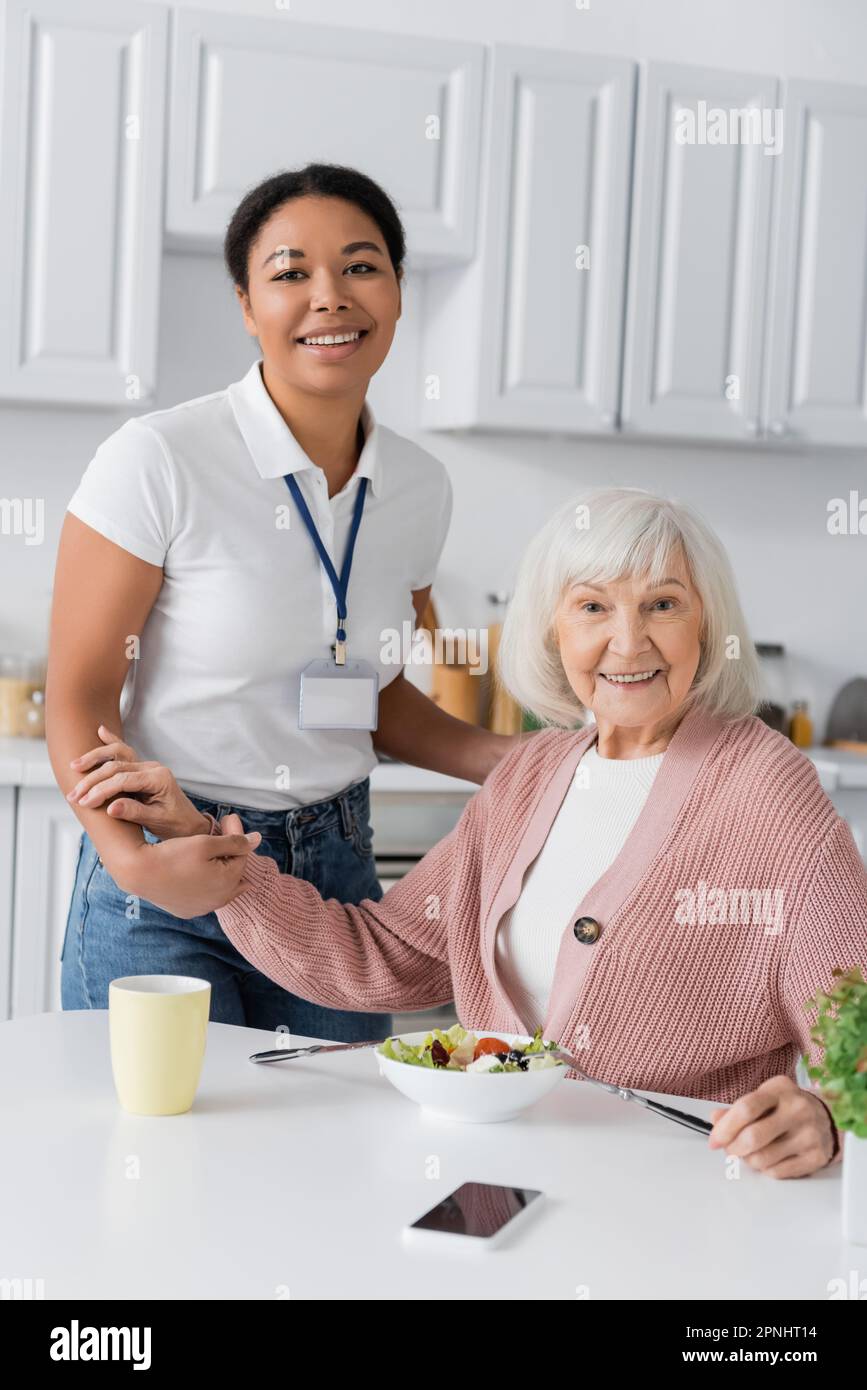happy multiracial social worker holding hands of thankful retired woman ...