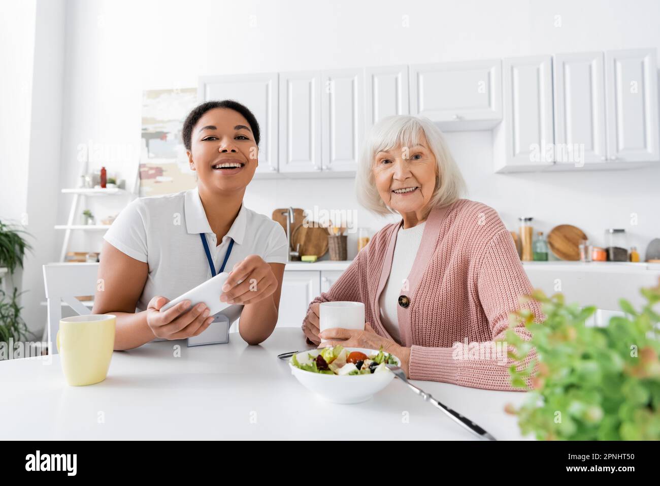 happy multiracial social worker holding smartphone during lunch with ...