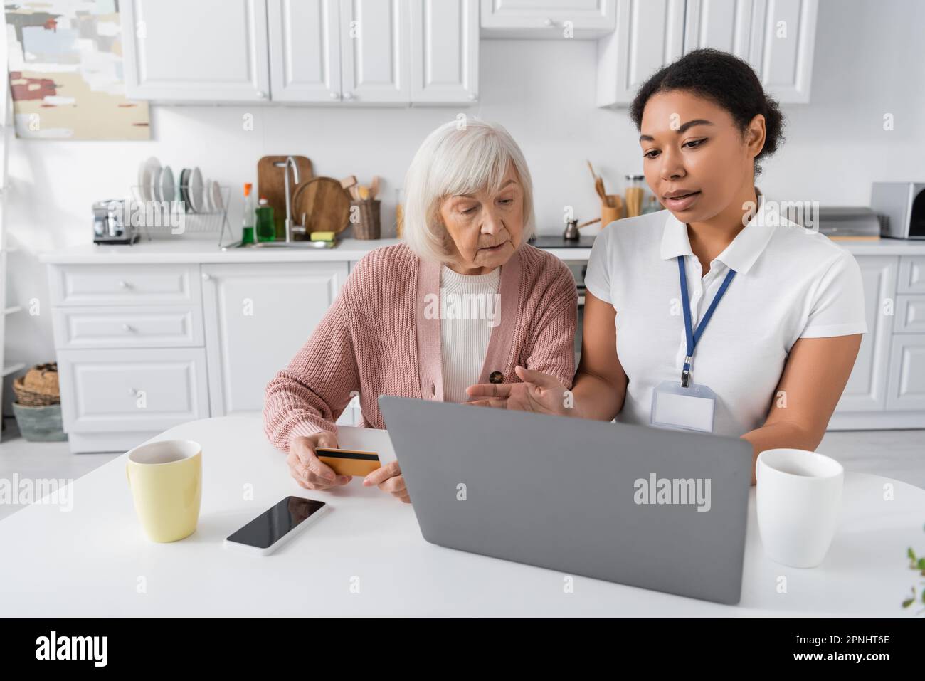 multiracial social worker using laptop while explaining senior woman ...