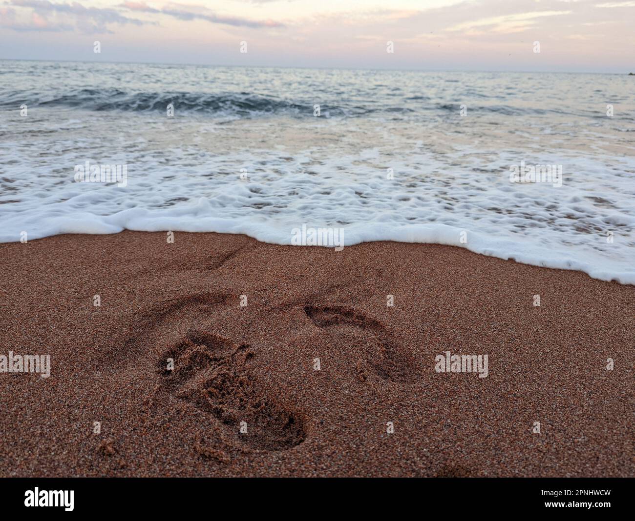 Two foot prints made in the sand of a beach, illuminated by the fading ...