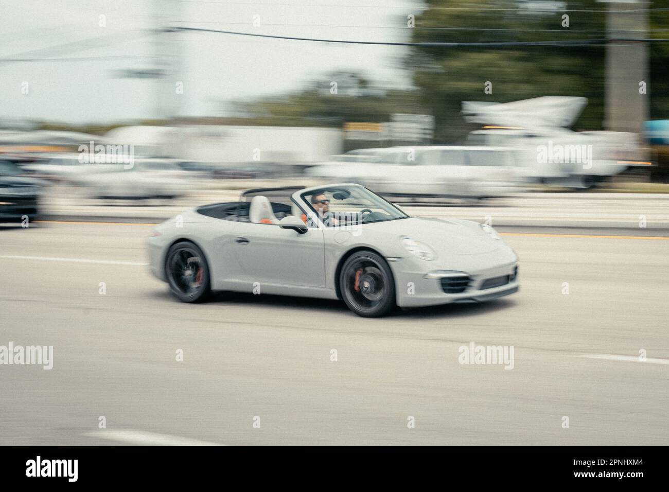 A white Porsche Cabriolet convertible sports car is driving down a busy ...