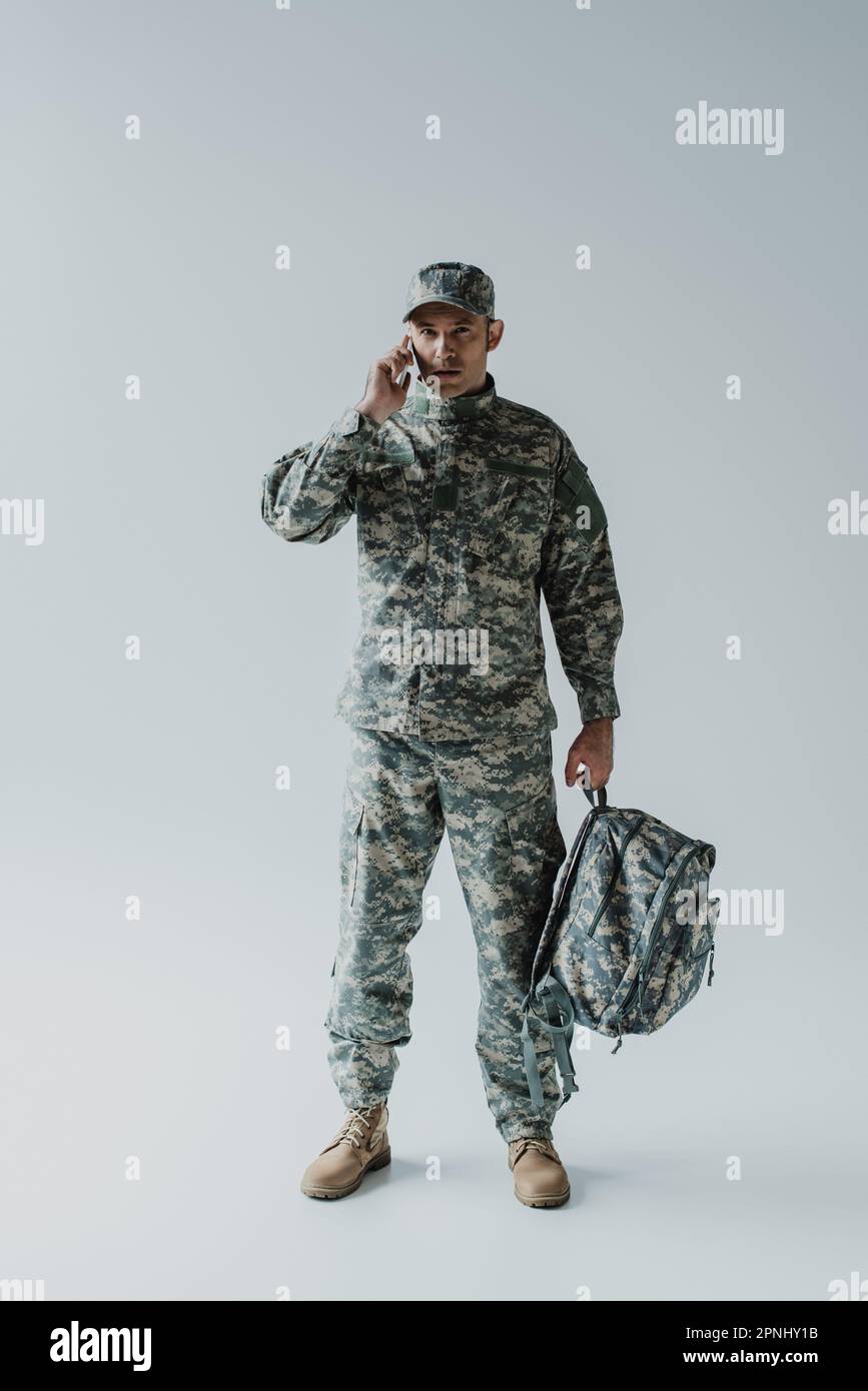 serviceman in cap and army uniform talking on smartphone while holding ...