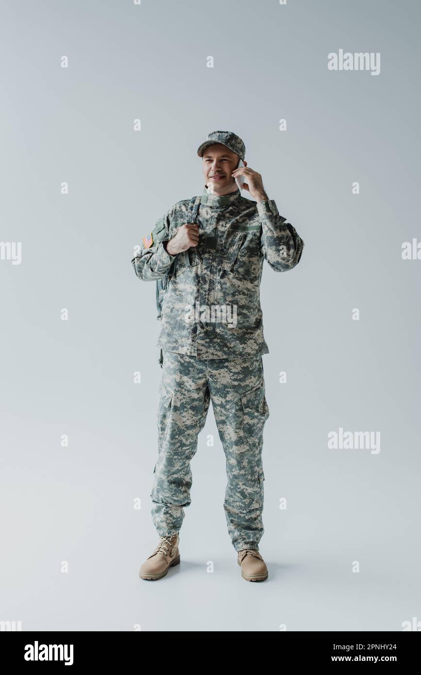 full length of happy serviceman in cap and uniform talking on ...