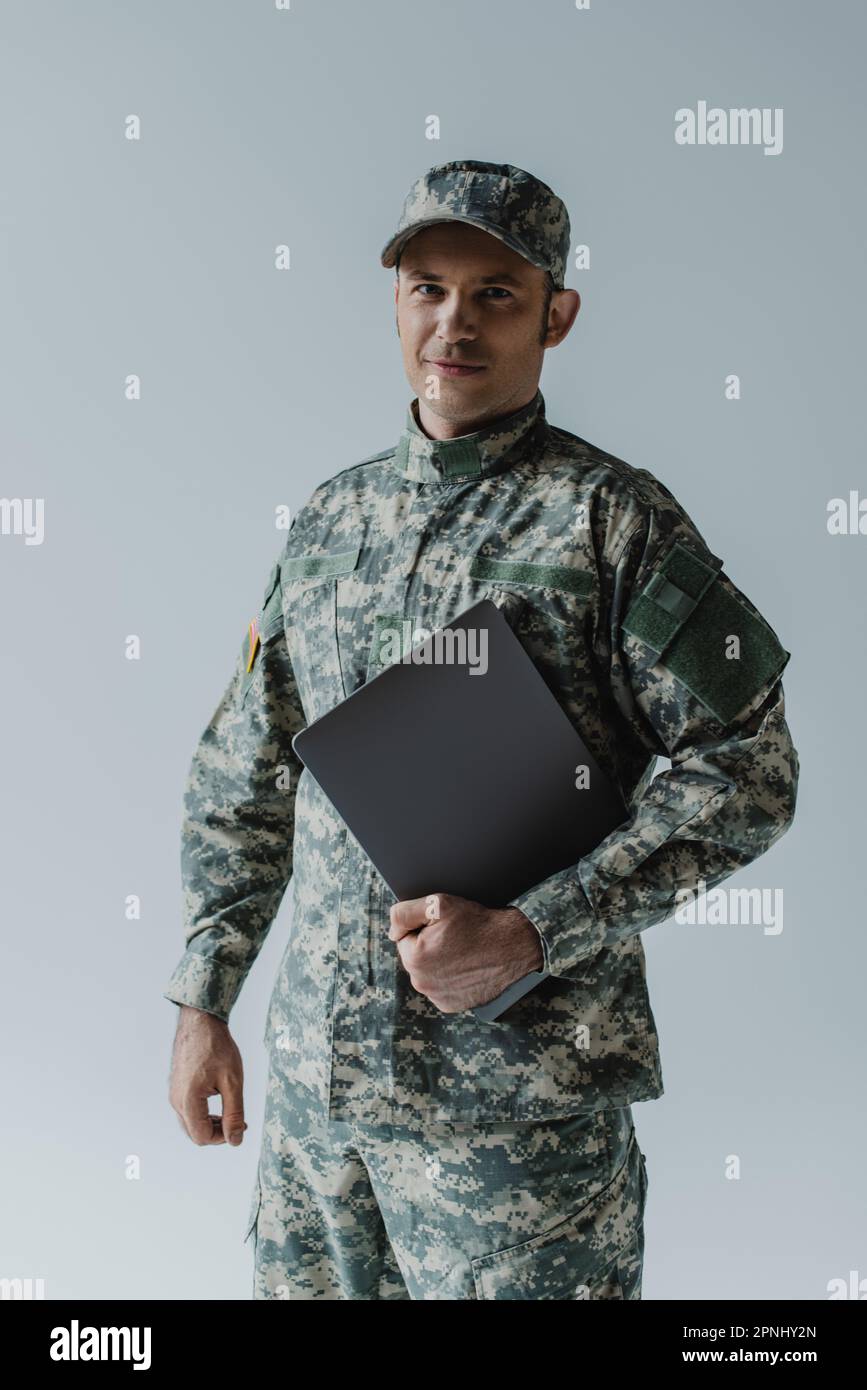 good looking soldier in army uniform and cap standing with laptop ...