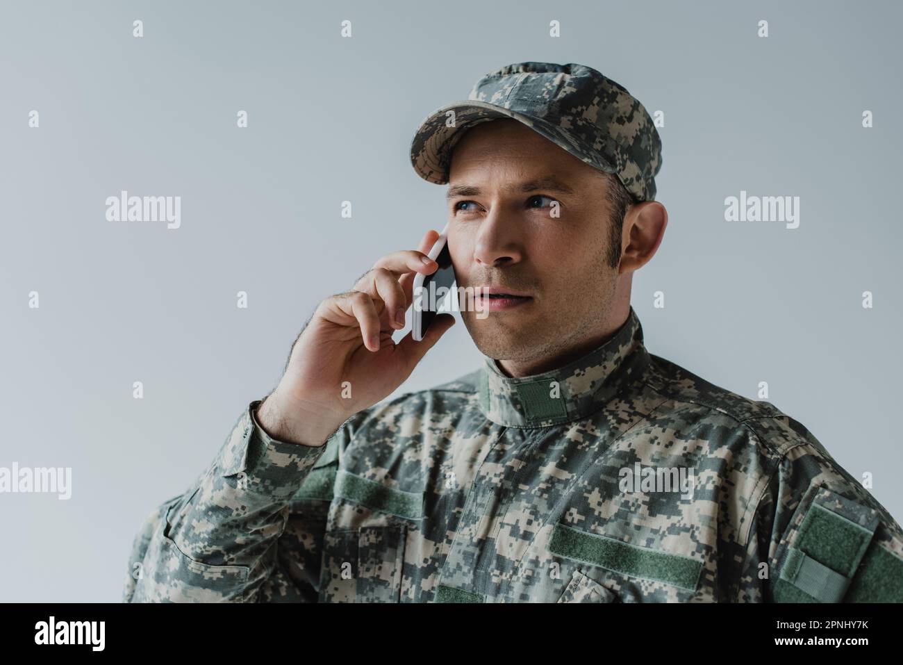 serviceman in cap and army uniform having conversation on smartphone ...