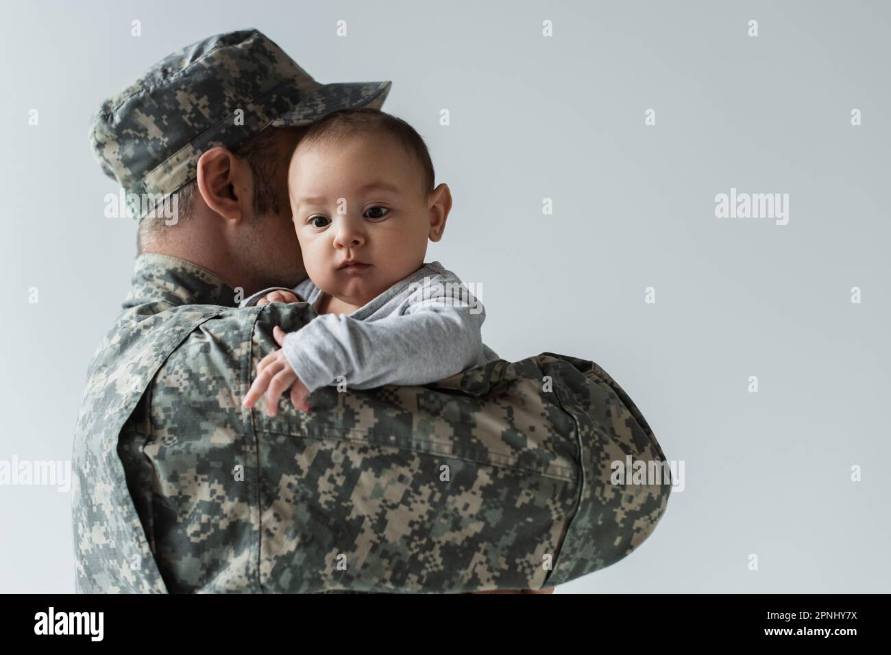 father in military uniform and cap hugging infant son isolated on grey ...