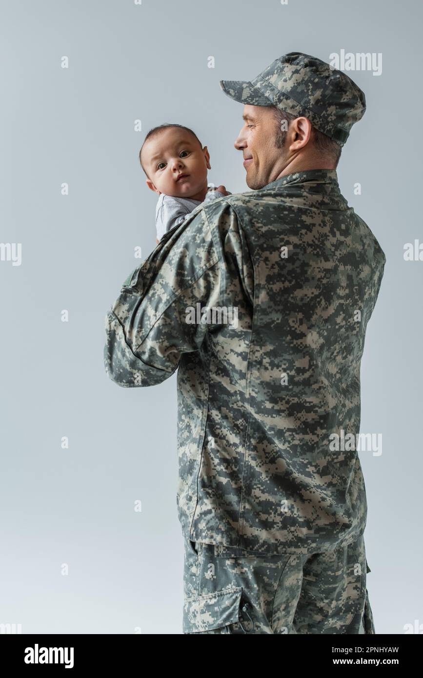 smiling army soldier in military uniform with cap holding infant son in ...