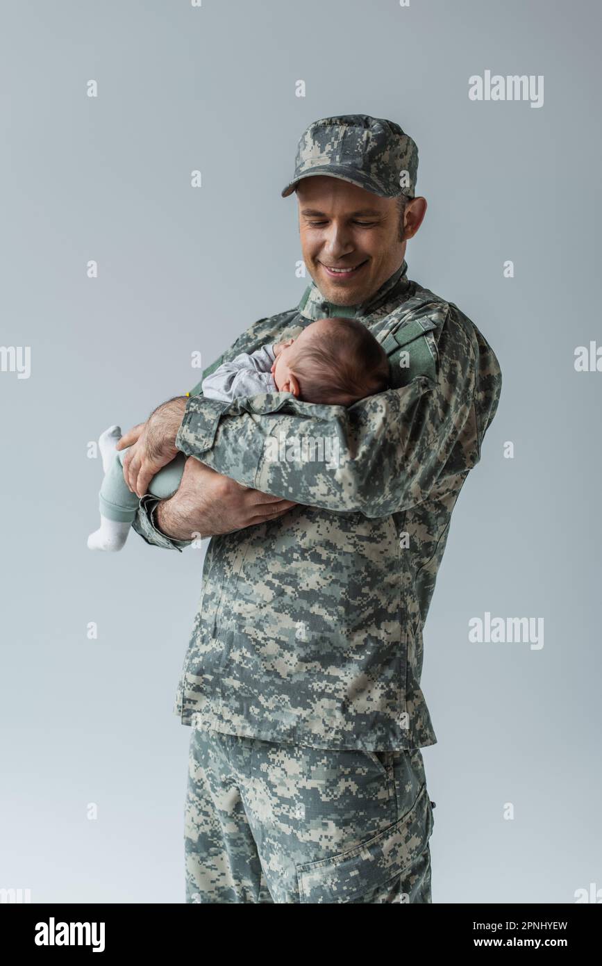 cheerful serviceman in uniform and cap holding newborn son isolated on ...