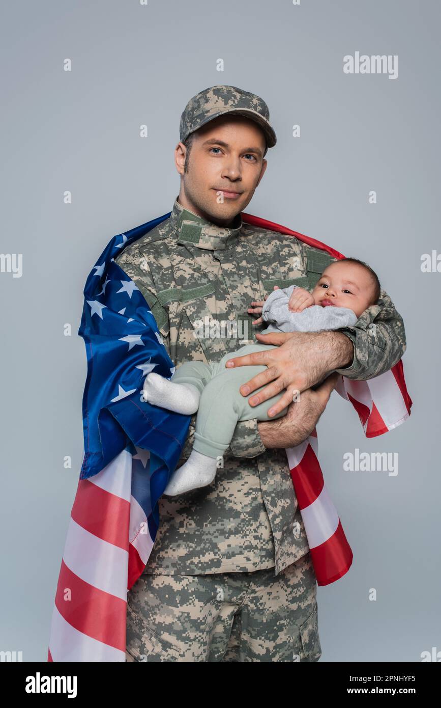 patriotic serviceman in uniform standing with American flag and holding ...