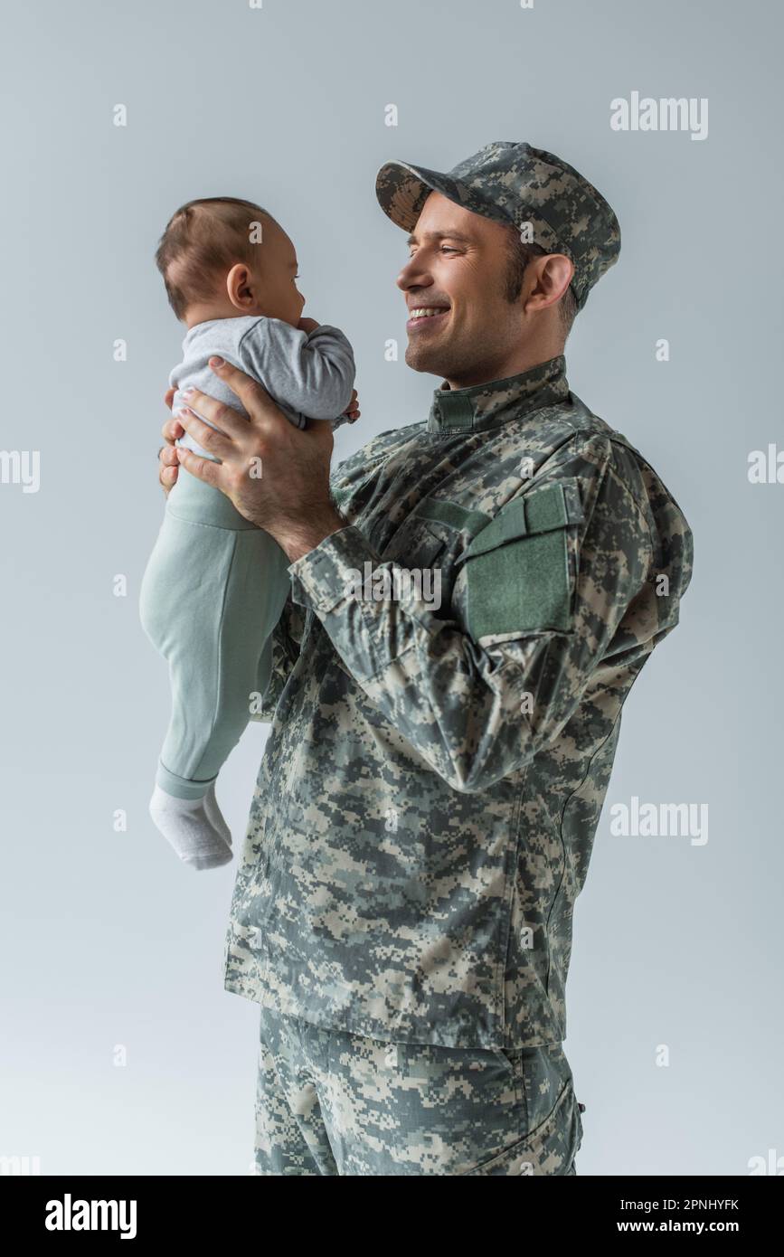 positive army soldier in uniform holding newborn son in arms isolated ...