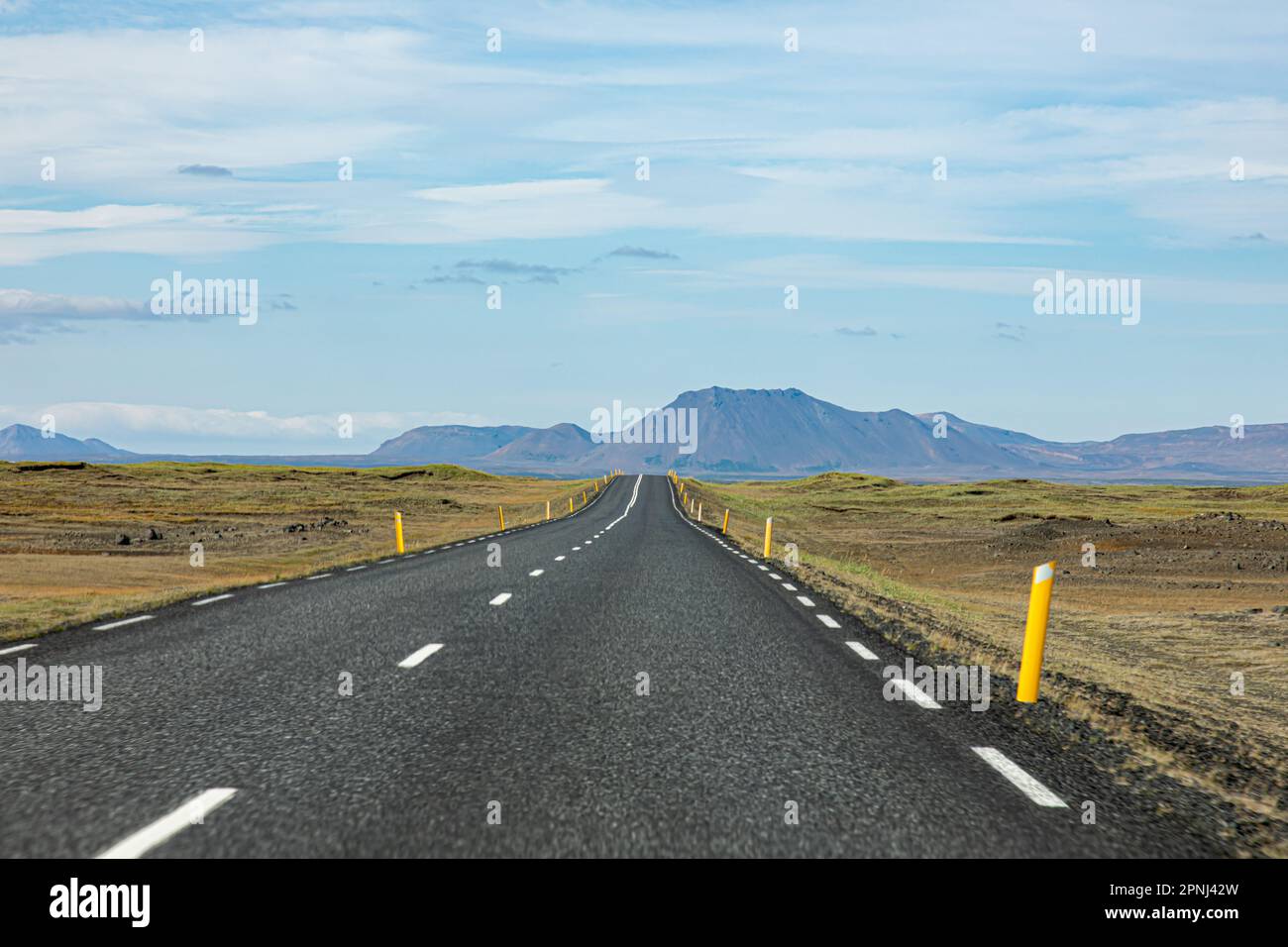 Long and empty road in the countryside of Iceland with mountains on the background and a ...
