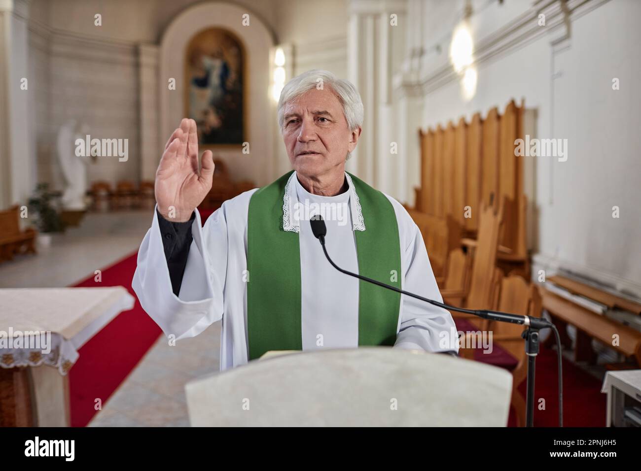 Senior priest in formal wear reading Bible in microphone while standing ...