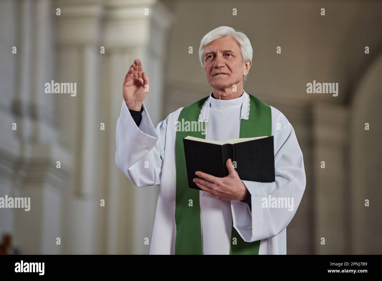 Senior priest holding Bible book reading prayers and blessing believers ...