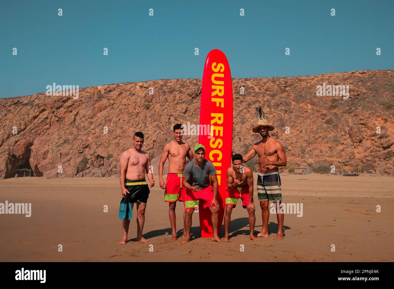 Five male lifeguards at Aftas Beach pose with a large red surfboard ...
