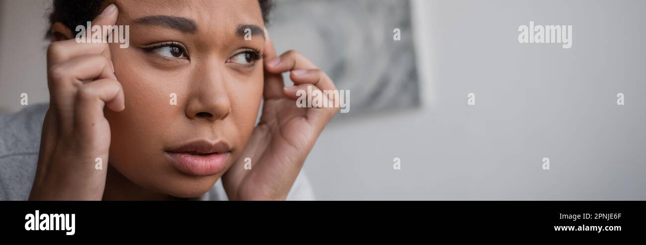 Depressed multiracial woman touching head and looking away at home ...