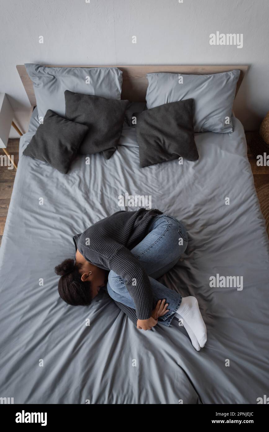 Top view of multiracial woman with depression lying on bed at home ...