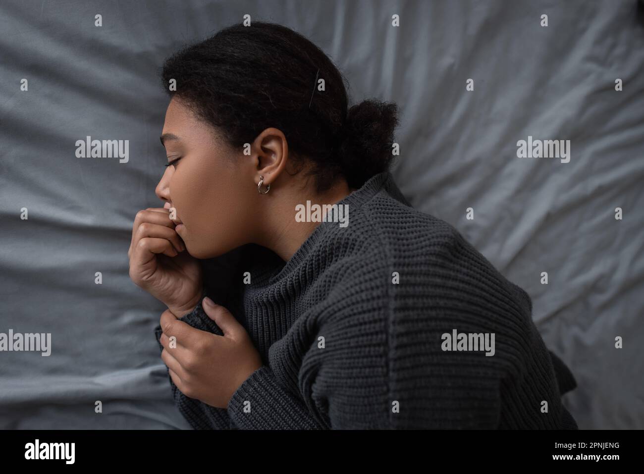 Top view of upset multiracial woman with depression lying on grey ...