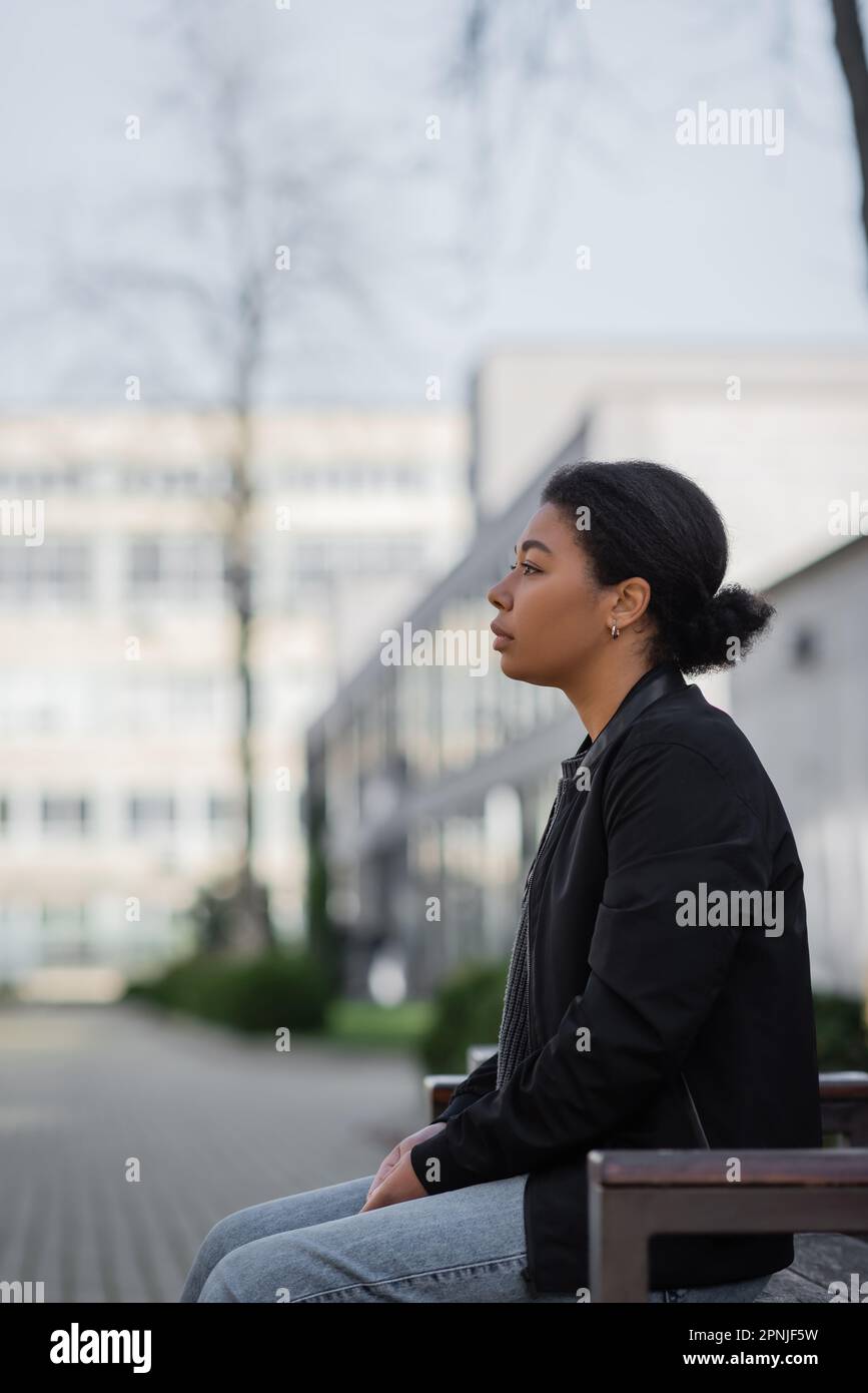 Side view of young multiracial woman with depression sitting on bench ...