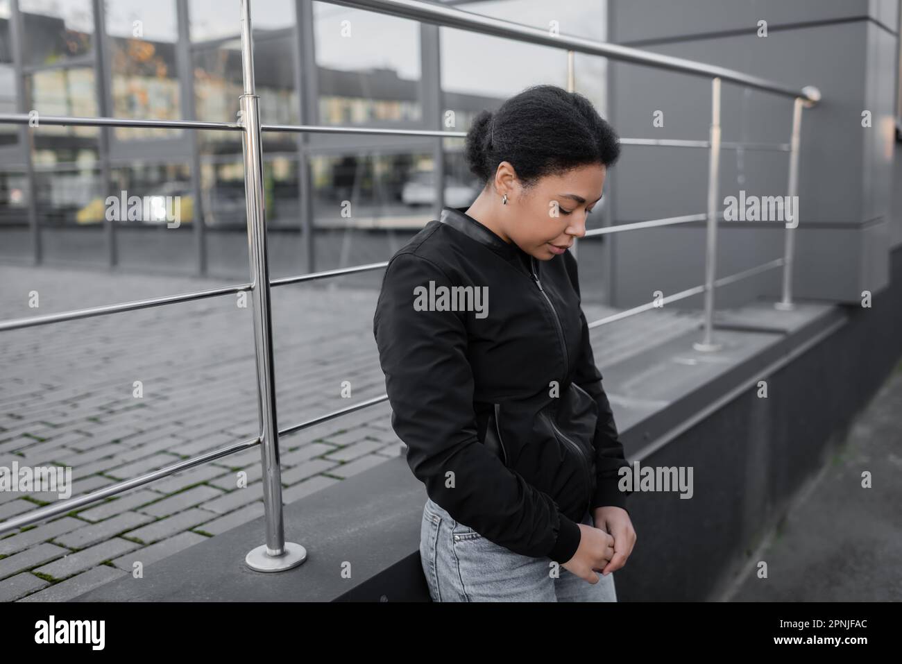 Young multiracial woman with apathy standing near building outdoors ...