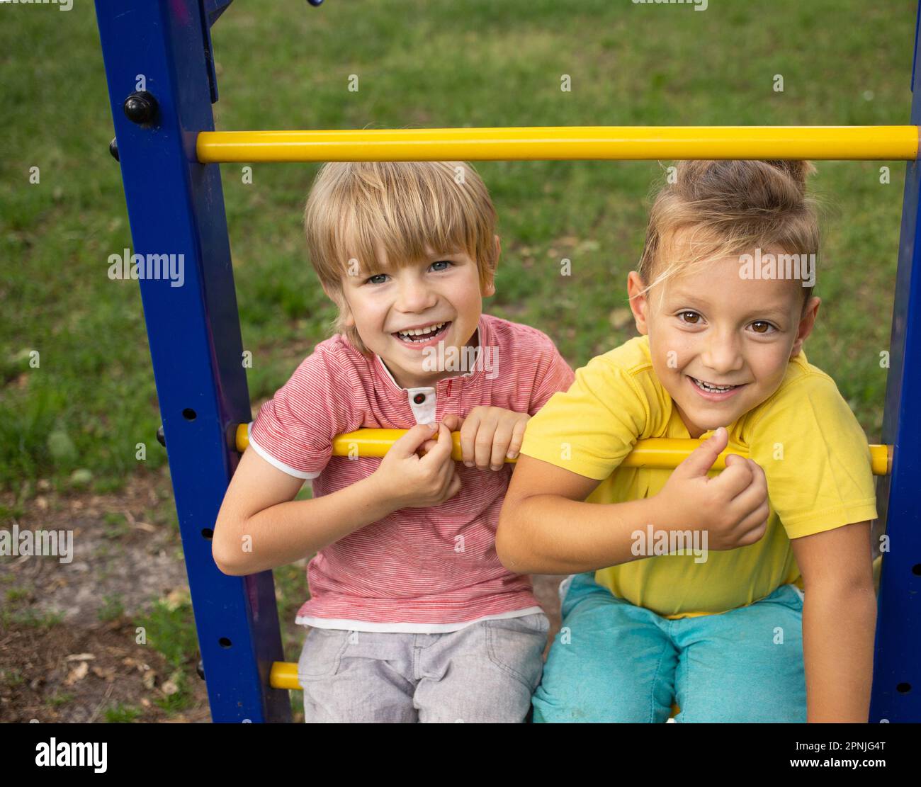 two 5-year-old boys are cute smiling while sitting on the playground in ...