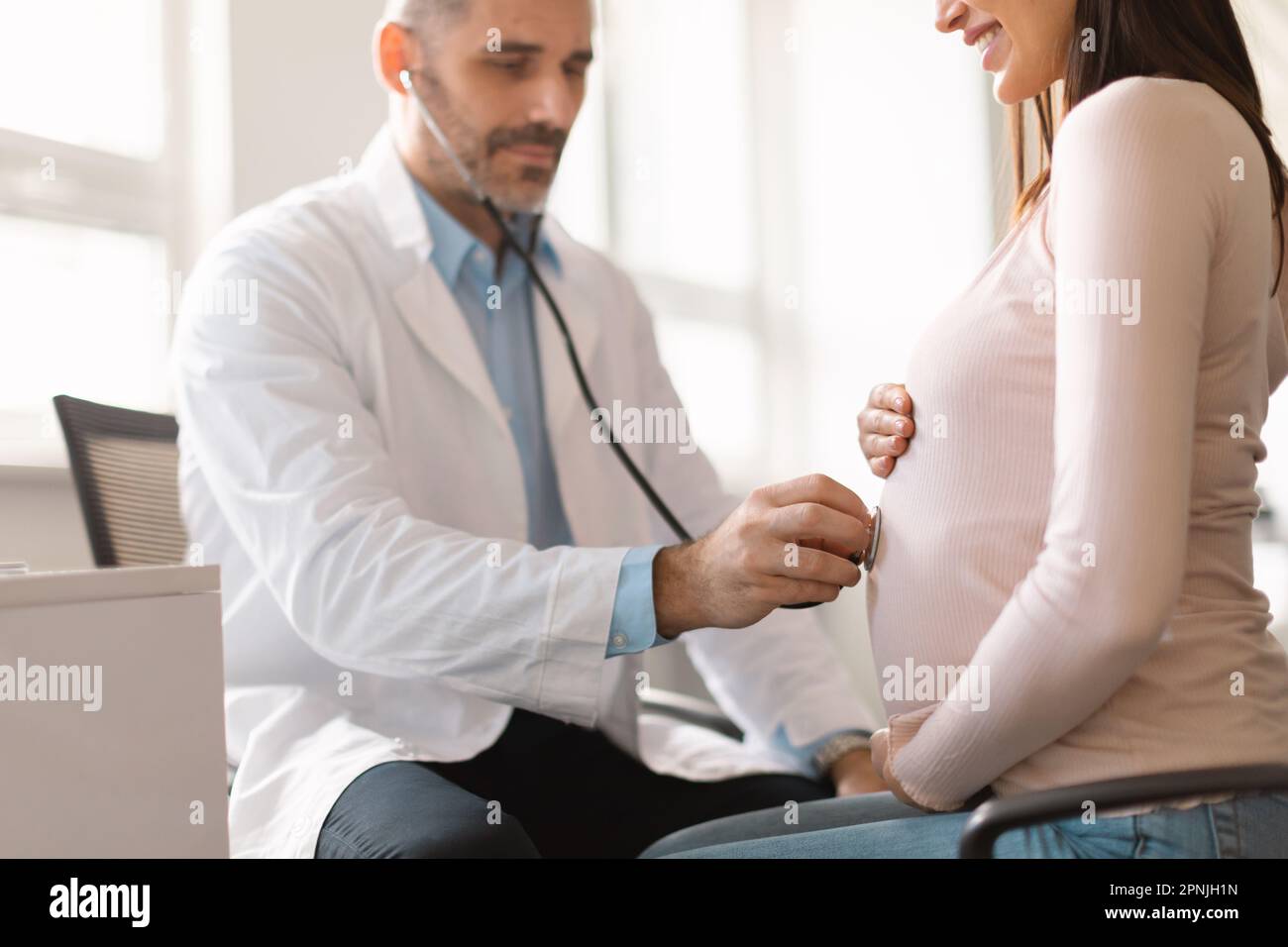 Male middle aged gynecologist with stethoscope examining belly of ...