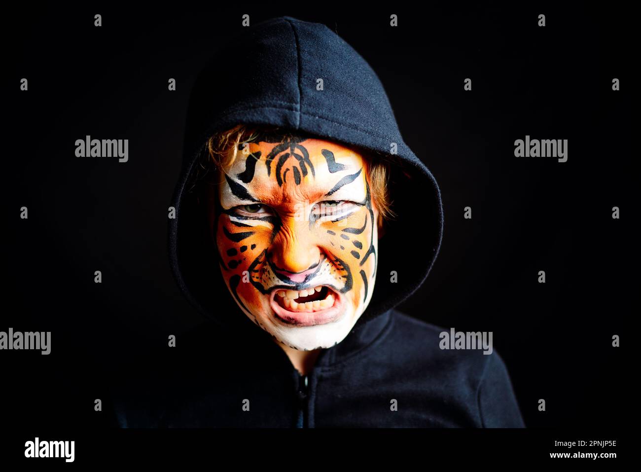 A growling boy with his face painted in the striking colors of a tiger ...