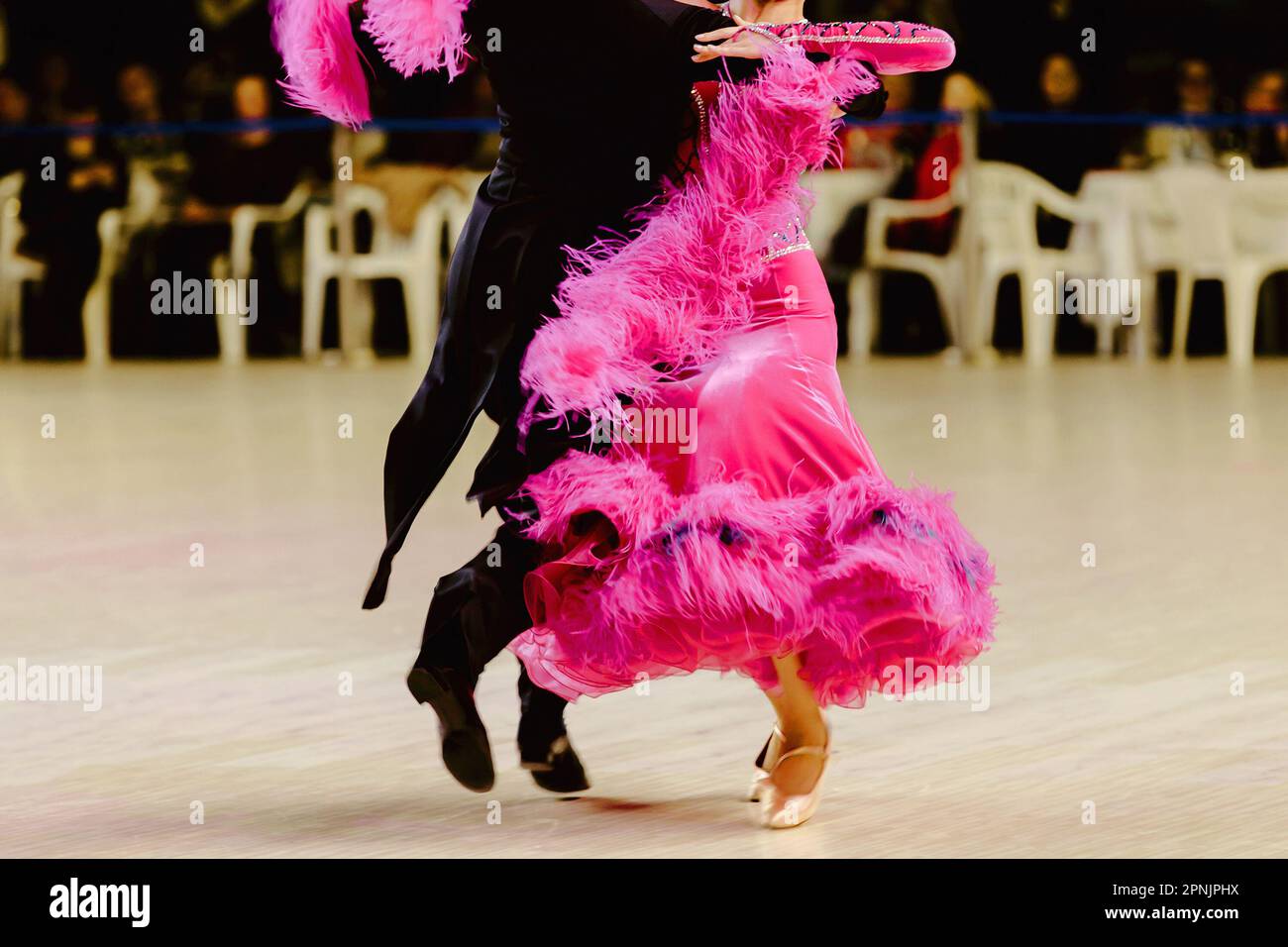 couple dancing foxtrot in competitive ballroom dancesport, woman is wearing pink dress and man ...