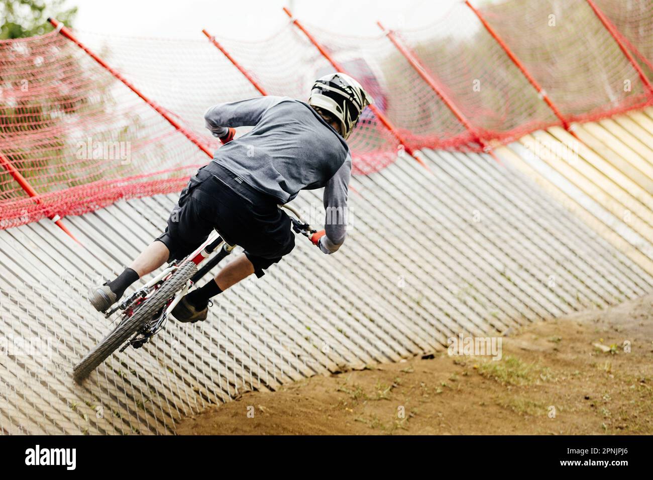 rear view mountainbiker rips turn on wood insloped corner in downhill ...