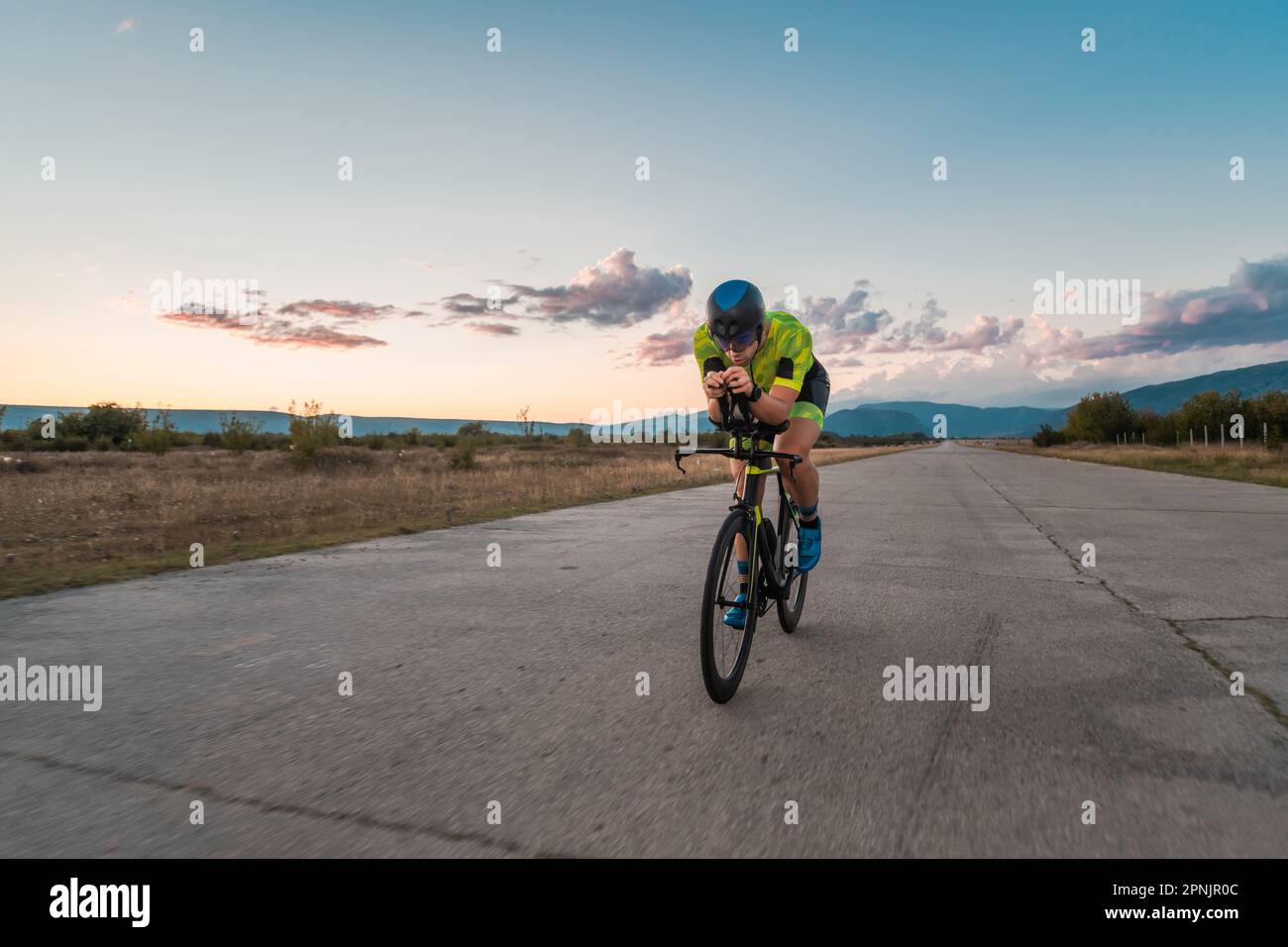 Triathlete riding his bicycle during sunset, preparing for a marathon ...