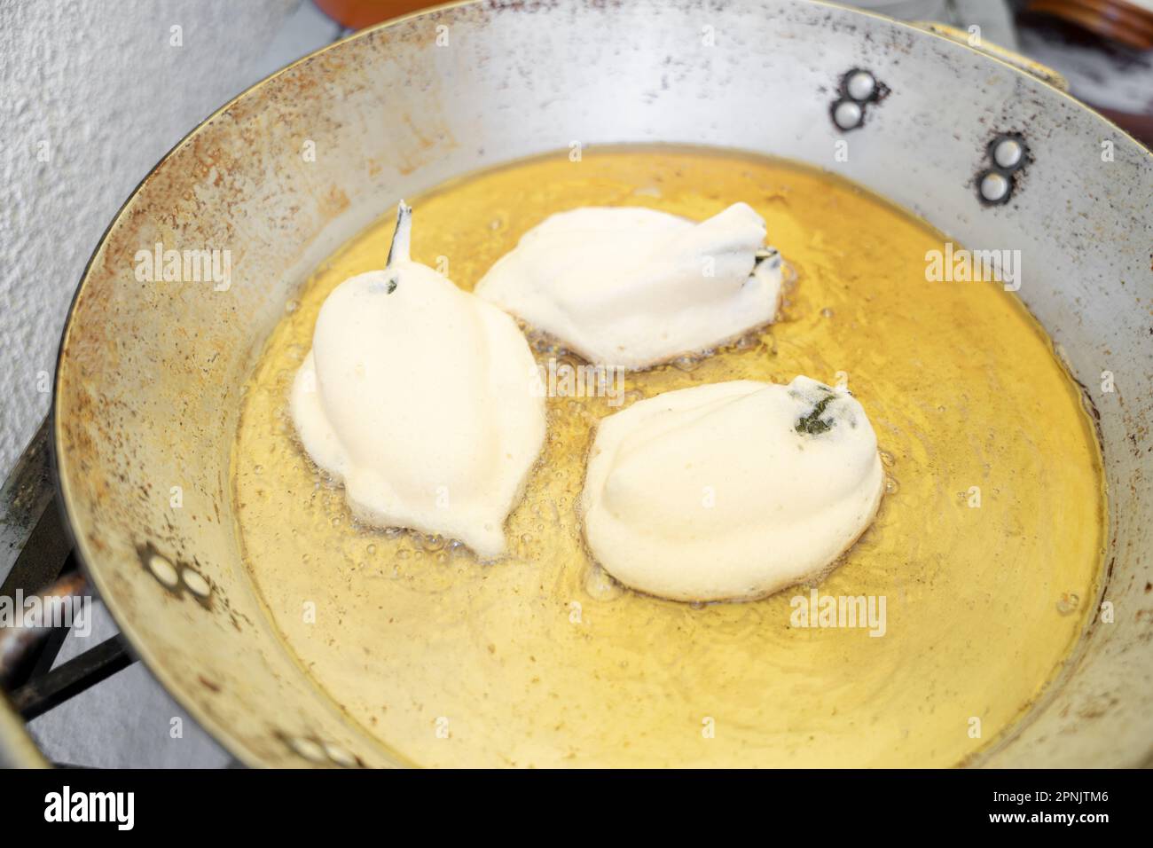 Three stuffed and battered poblano chilli peppers are being fried in a ...