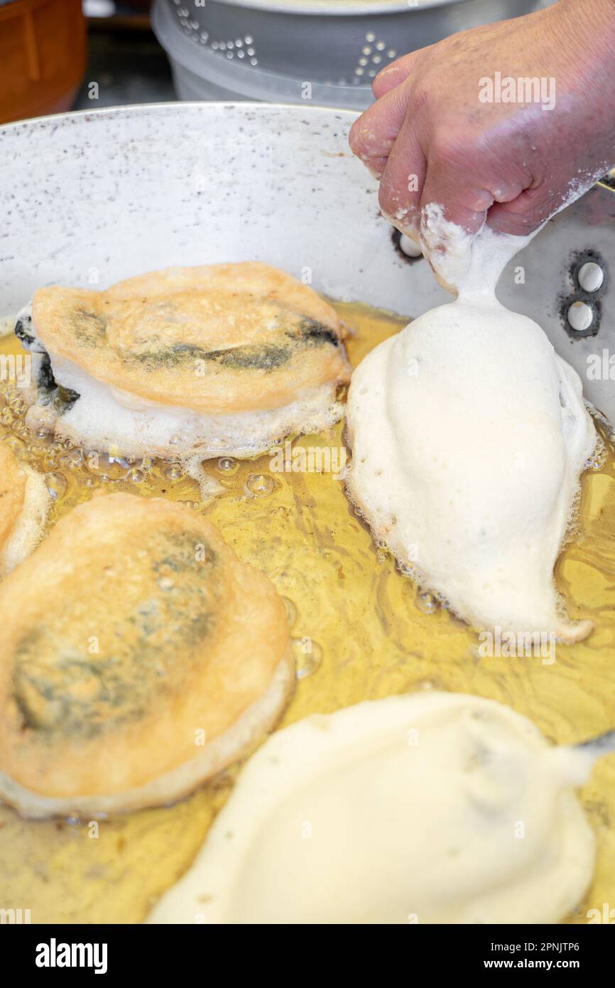 An adult Hispanic woman is frying battered poblano chilli peppers in a ...