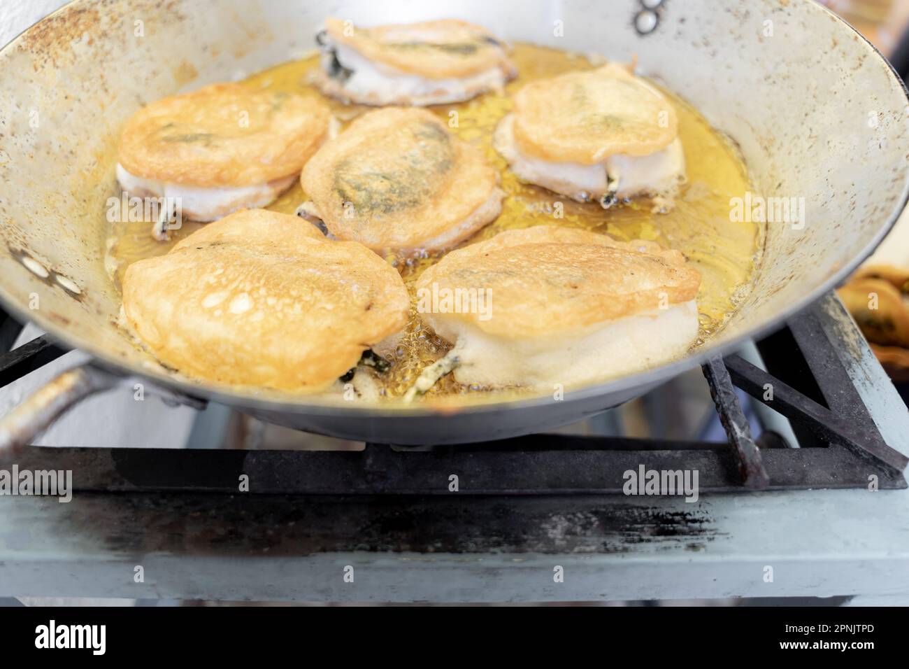 Some stuffed and battered poblano chilli peppers are being fried in a ...