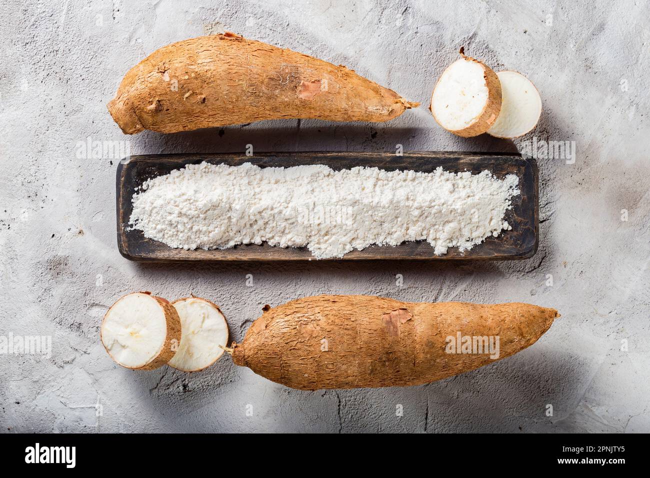 pile of cassava root and cassava flour on a gray and white textured ...