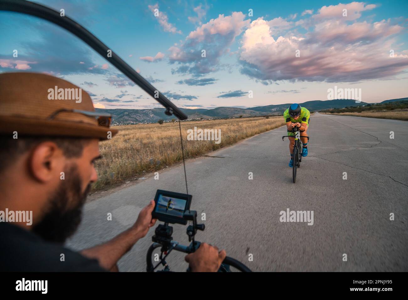 A videographer recording a triathlete riding his bike preparing for an ...