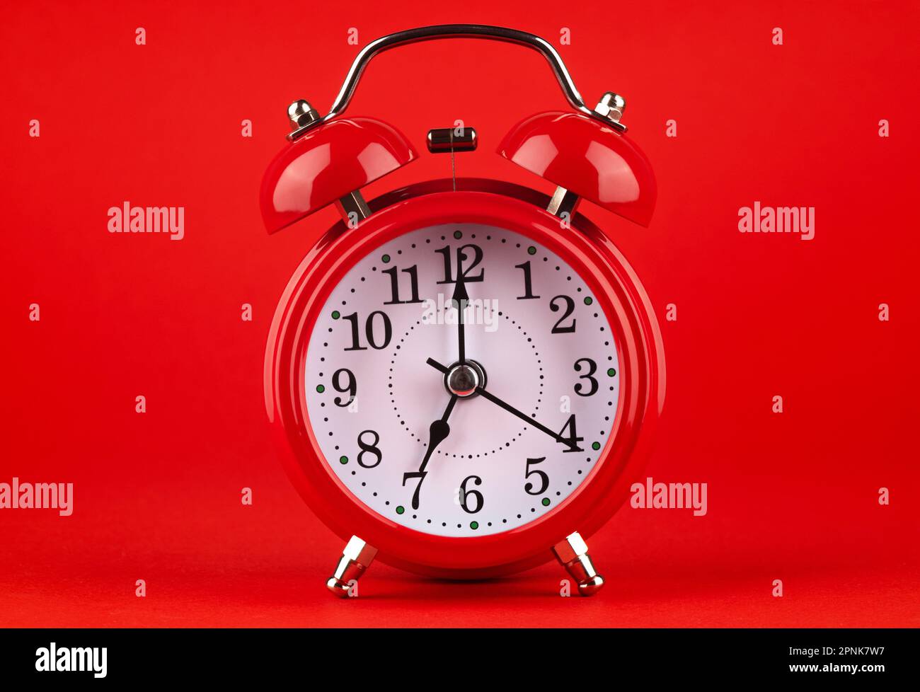 Red alarm clock on a red background. It's 7 o'clock on the clock ...
