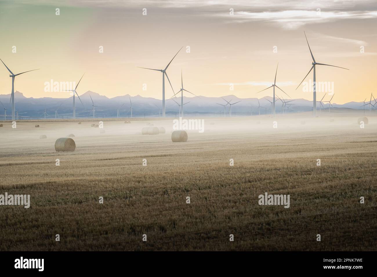 Windmill scene on a prairie landscape overlooking round hay bales with ...