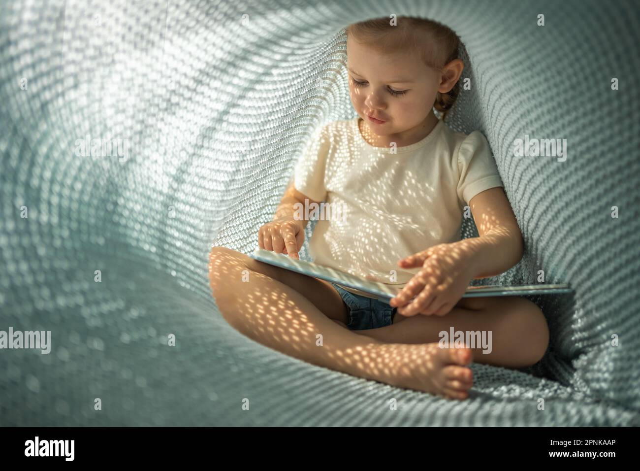 Little girl enjoying of review a book under blue knitted plaid in sunny ...