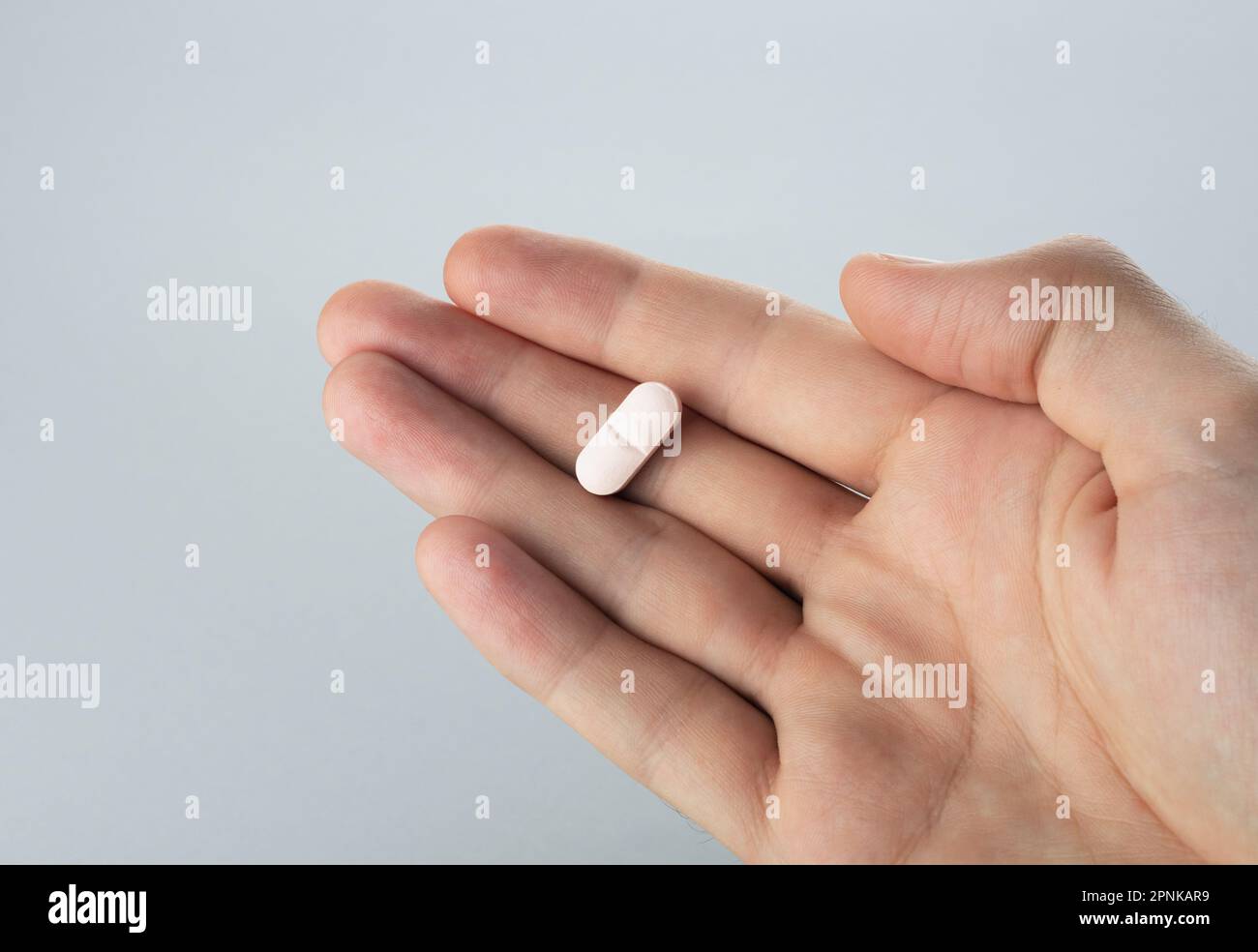 Male hand holding a white pill on a grey background. Close up Stock ...