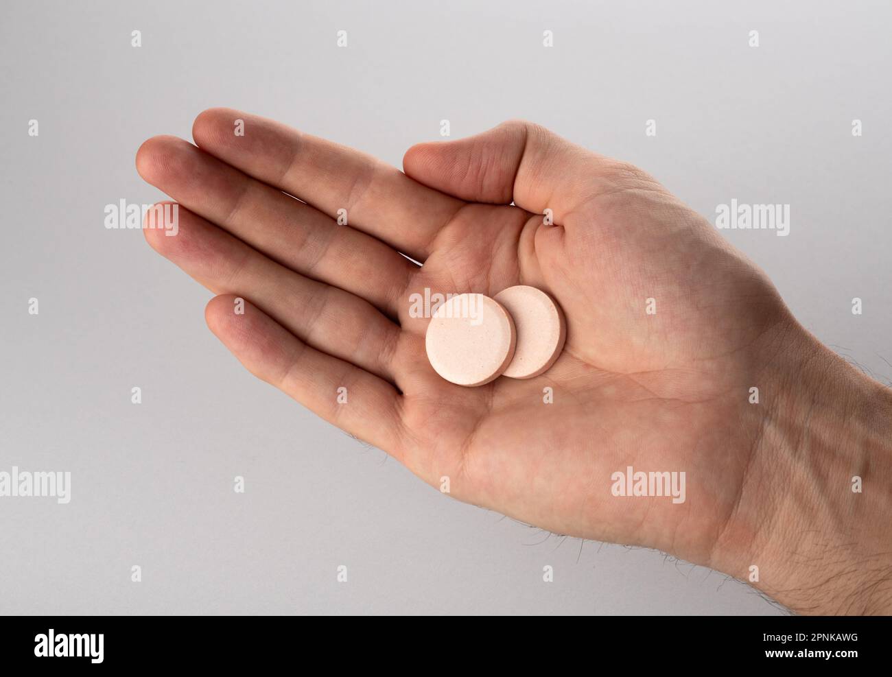 Male hand holding two effervescent tablets in hand on grey background ...