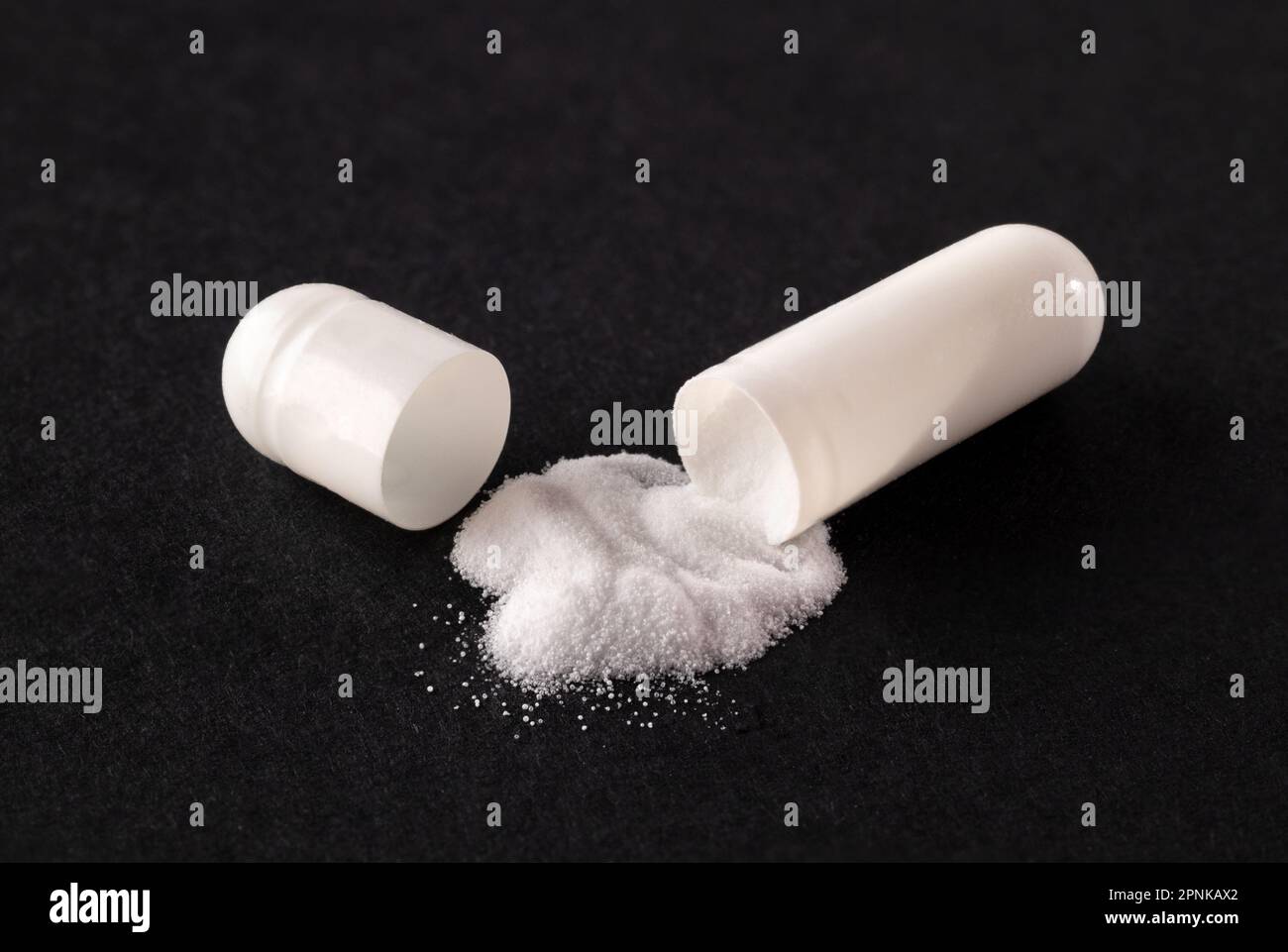 A white pill on a black background. An open pill with its contents ...