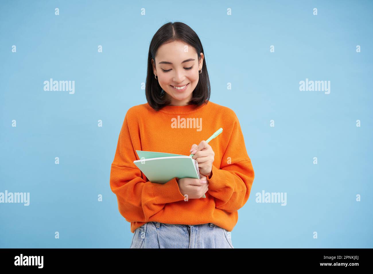 Smiling cute girl student, making notes, writing down homework ...