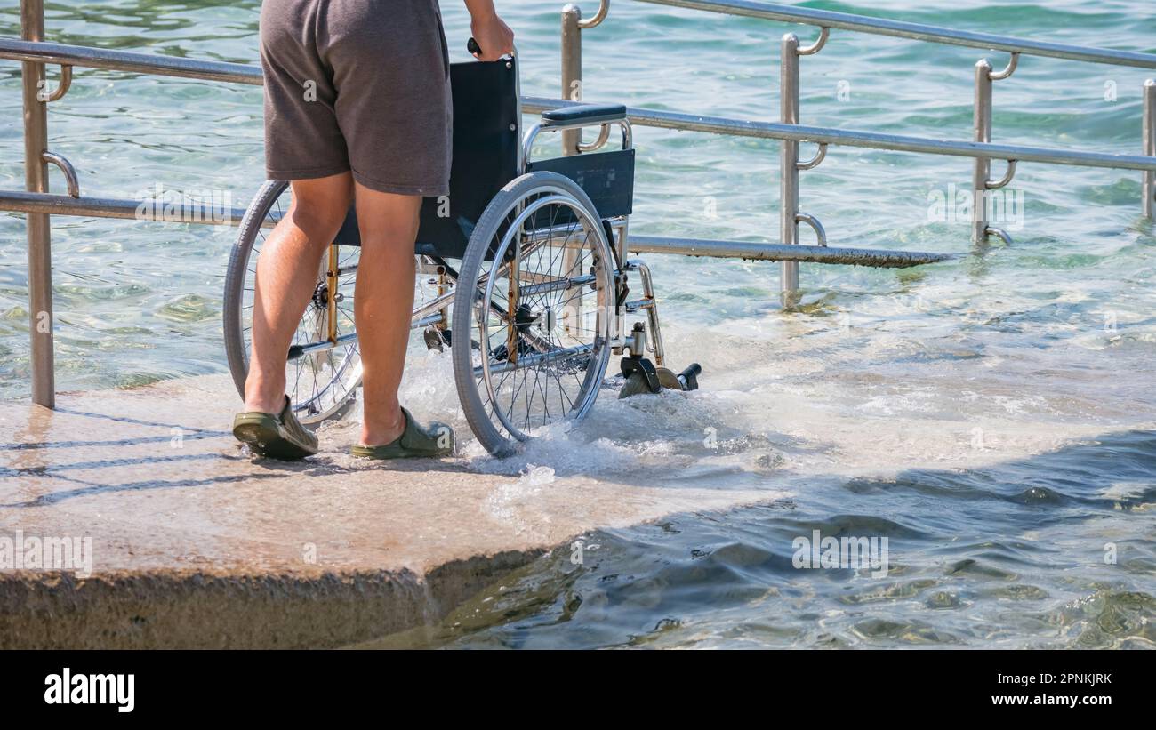 Lifeguard pushing wheelchair at sea on accessible beach with ramp for ...