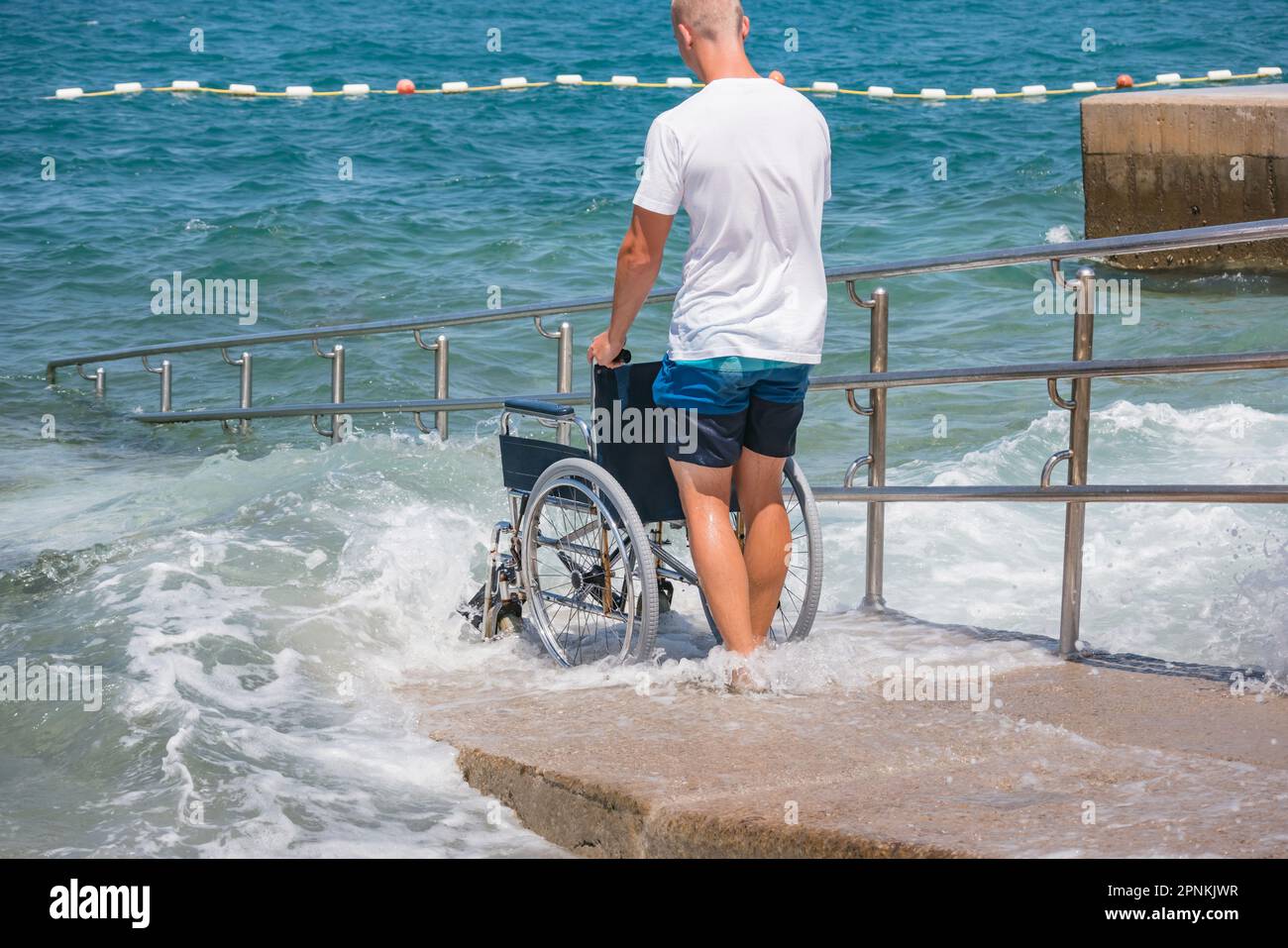 Lifeguard pushing wheelchair at sea on accessible beach with ramp for ...
