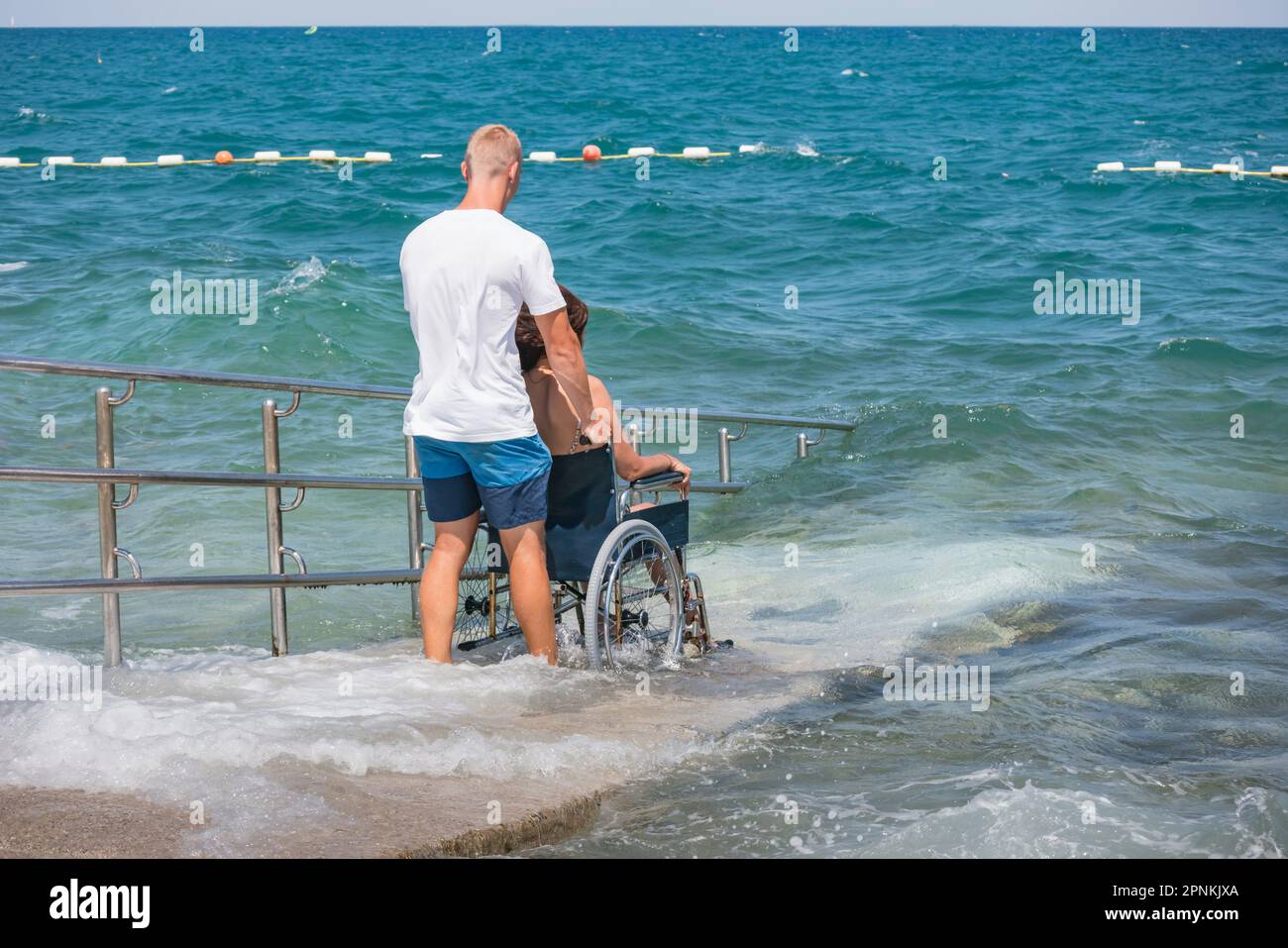 Woman with disability at beach goes to swimm on a wheelchair with ...
