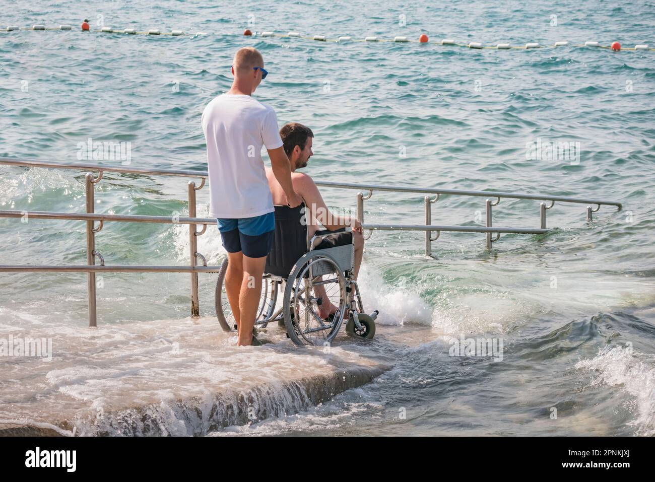 Man with disability at beach goes to swimm on a wheelchair with ...